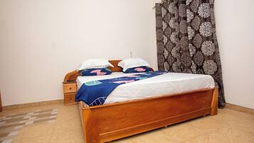 Quarto com cama de madeira, mesa de cabeceira, gaveta e cortina estampada.