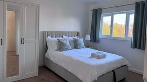 Quarto com cama, mesa de cabeceira, janela com cortinas e guarda-roupa.