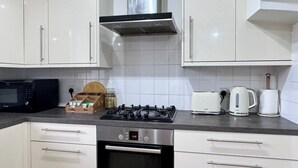 Uma cozinha com armários brancos, micro-ondas preto, fogão a gás, torradeira e cafeteira.
