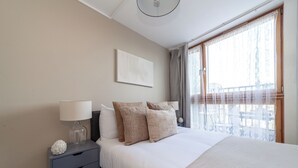 Quarto com uma cama grande, mesa de cabeceira com abajur e vista para uma varanda.