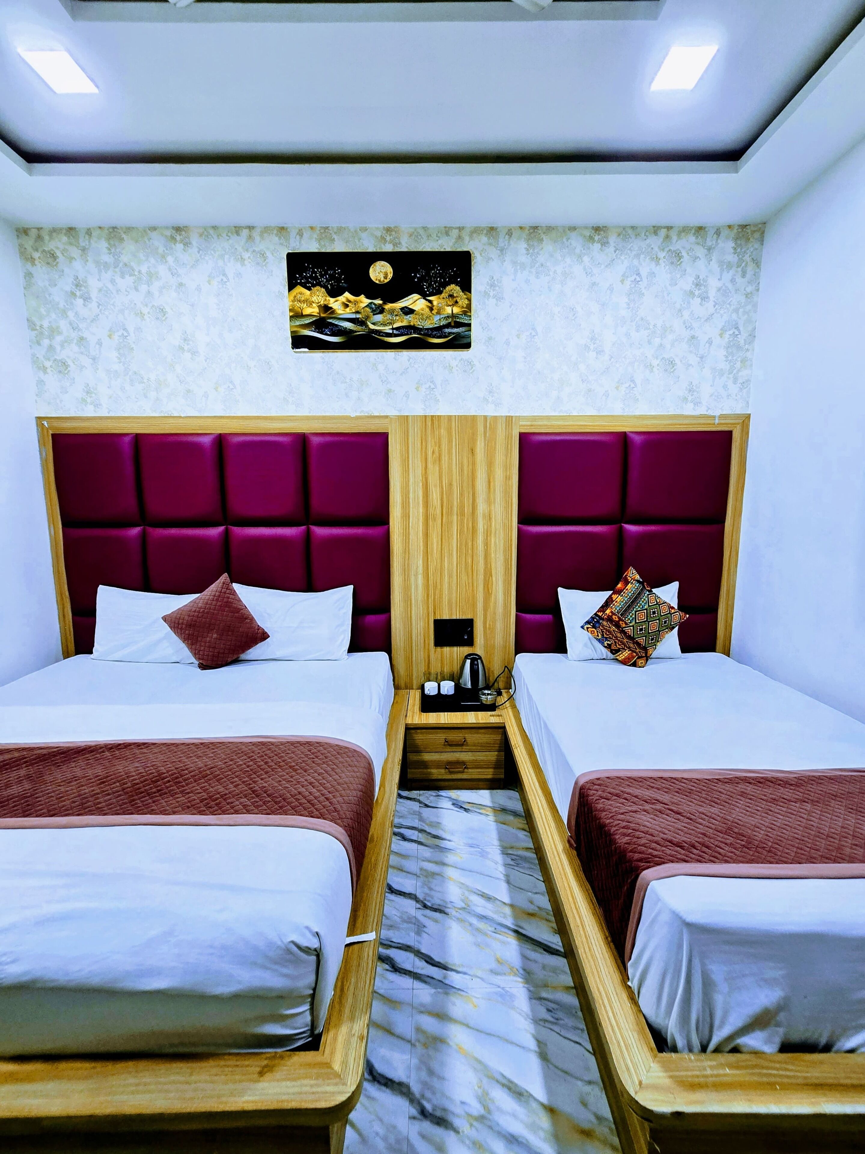 Quarto de hotel com duas camas, uma cabeceira de madeira, mesa de cabeceira e uma obra de arte na parede.