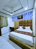 Quarto de hotel com cama, escrivaninha, cadeira, ventilador de teto e parede com padrão de nuvens.