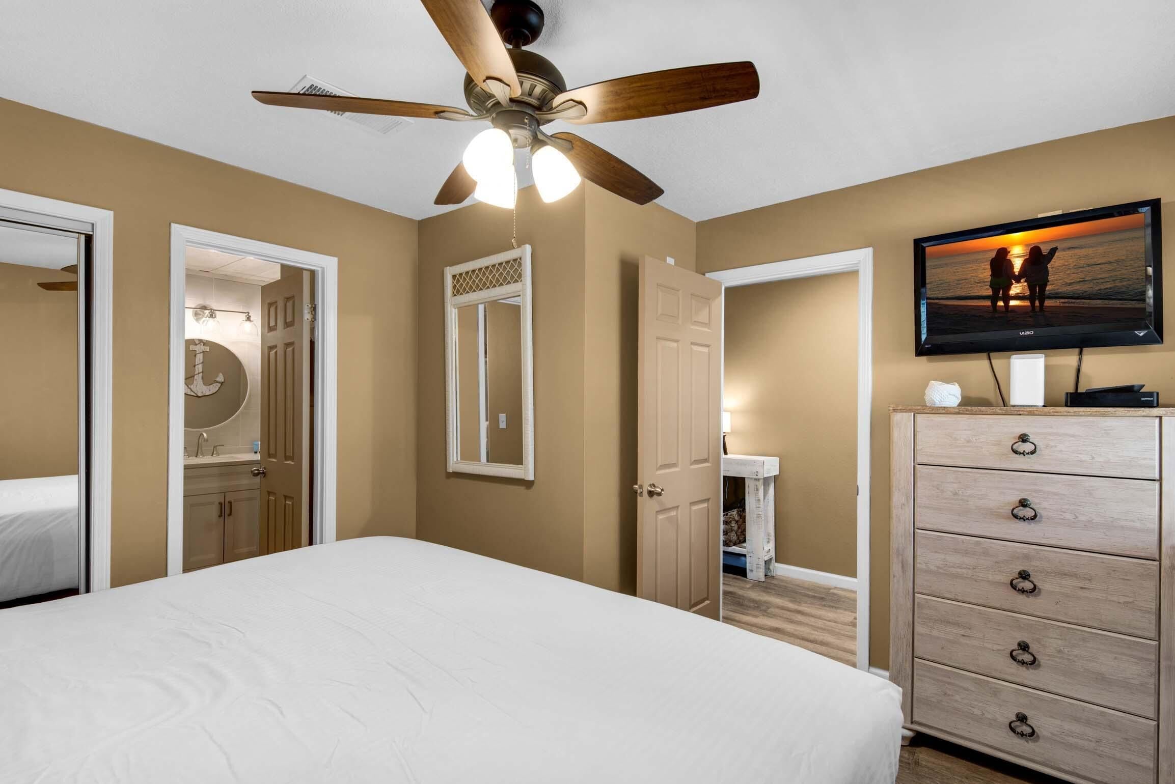 Quarto com cama, ventilador de teto, televisão e cômoda.