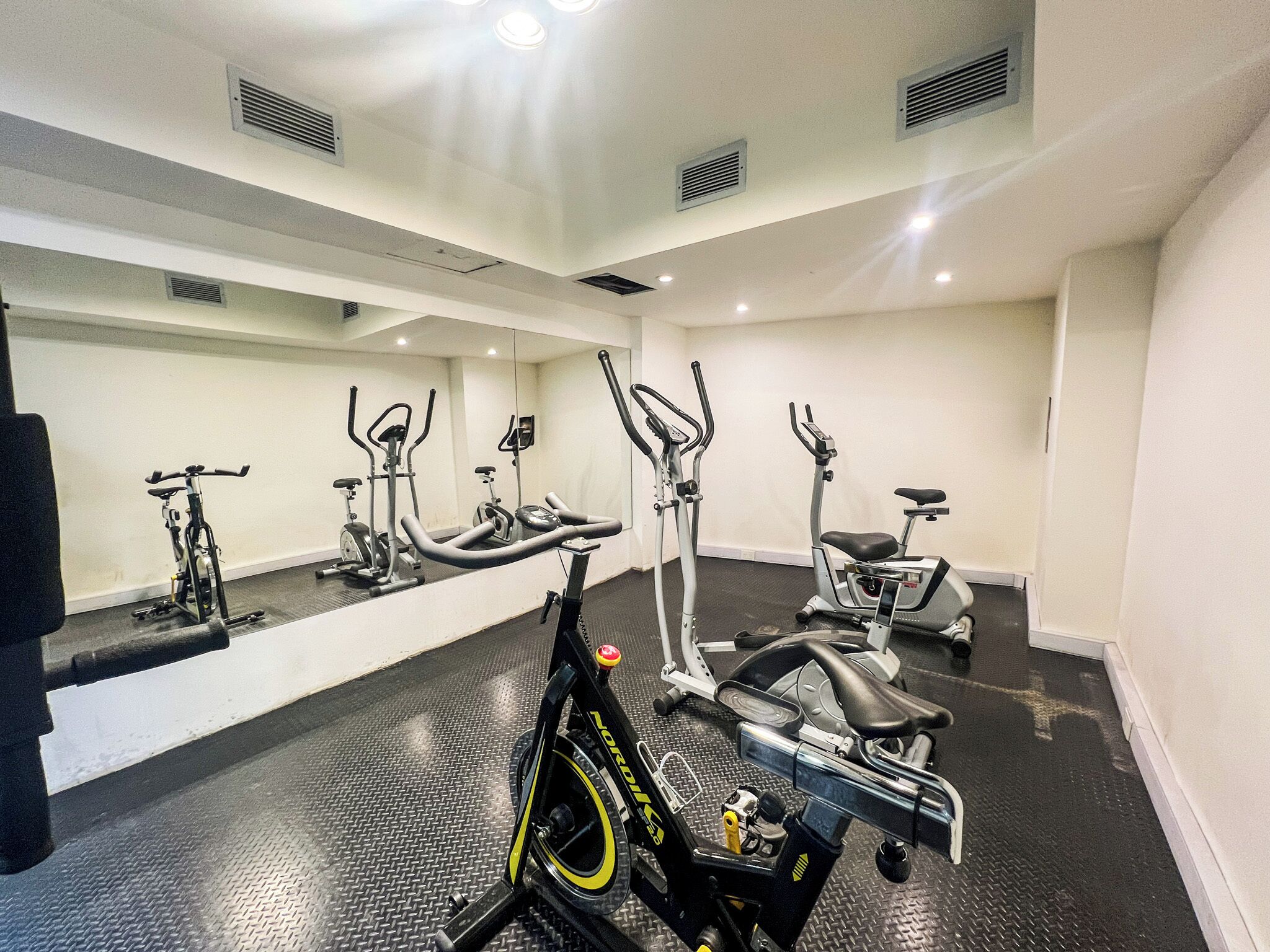 Uma academia com diversos equipamentos de exercício, um espelho e piso emborrachado.