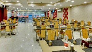 Uma sala de jantar ampla com várias mesas e cadeiras, piso limpo e entrada visível para outra área.