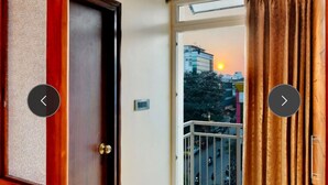 Quarto com porta de madeira, janela com cortinas e vista para o horizonte urbano ao pôr do sol.