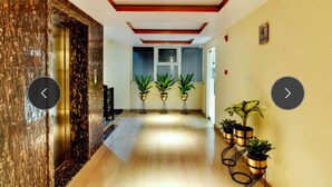 Um corredor com parede de mármore, piso de madeira e plantas em vasos.