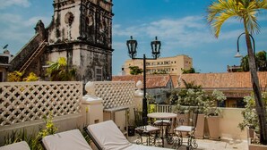 Terraço no telhado com cadeiras de descanso, uma mesa e plantas em vasos.