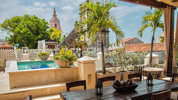 Terraço no telhado com piscina, área de refeições e vista para edifícios históricos.