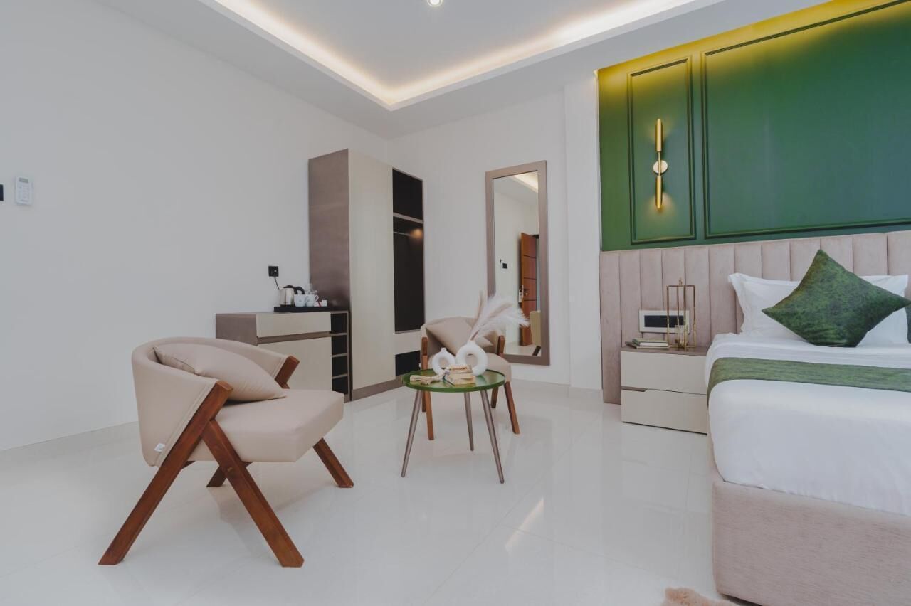 Quarto de hotel moderno com cama, uma cadeira, uma mesinha, guarda-roupa e espelho.