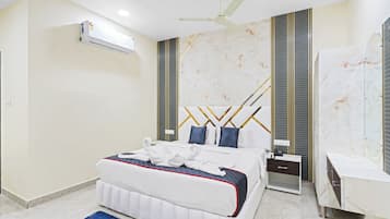 Quarto de hotel moderno com uma cama grande, uma mesinha de cabeceira, televisão integrada e banheiro com espelho e pia.