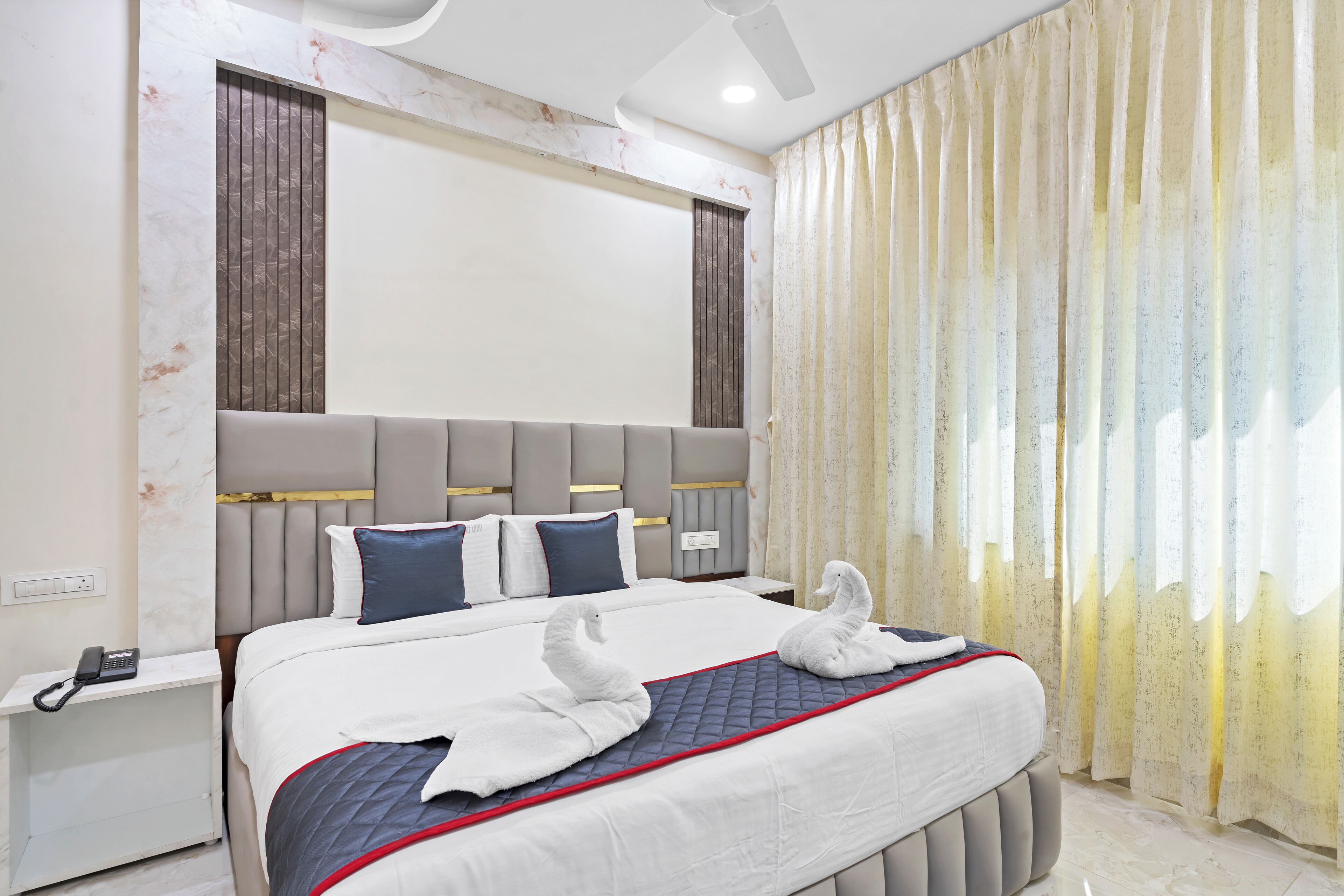 Quarto de hotel moderno com uma cama grande, telefone ao lado da cama e cortina com padrão discreto.