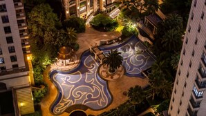 Vista aérea de um pátio arborizado com uma fonte, palmeiras e um gazebo.