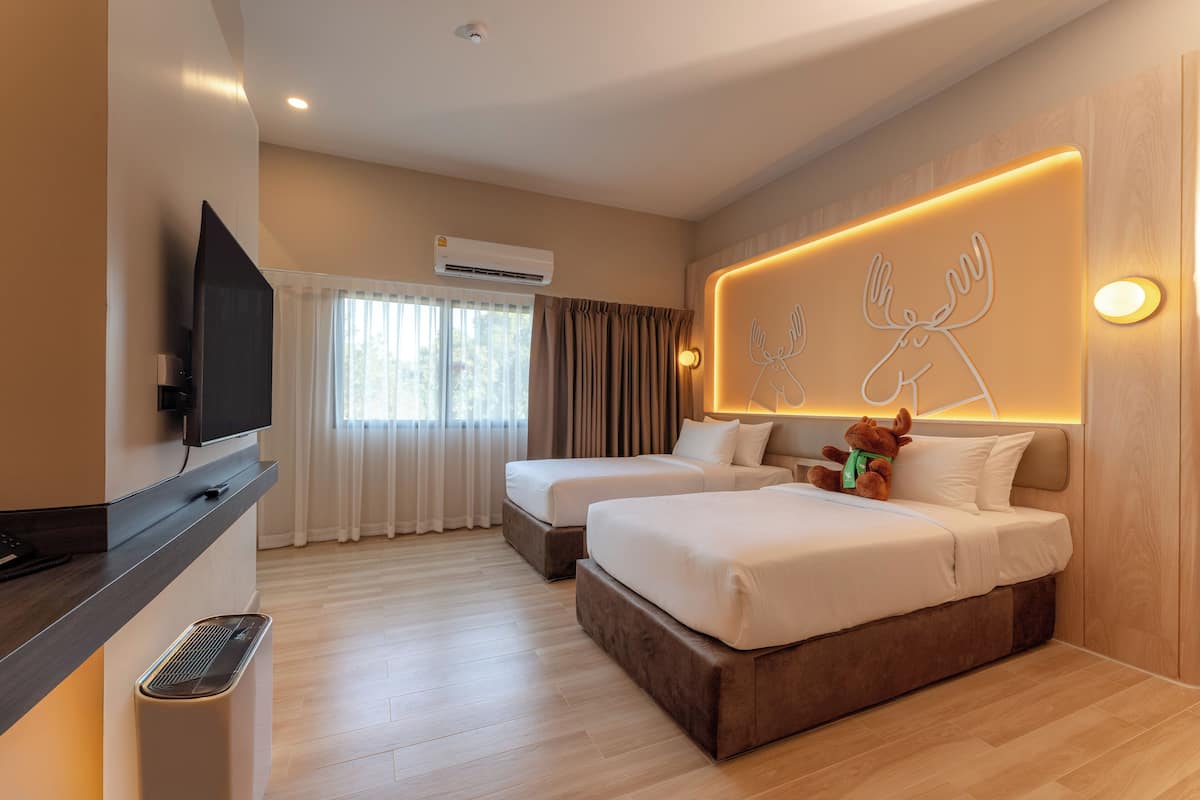 Quarto de hotel com duas camas, televisão de tela plana, ar condicionado e um objeto decorativo na parede.