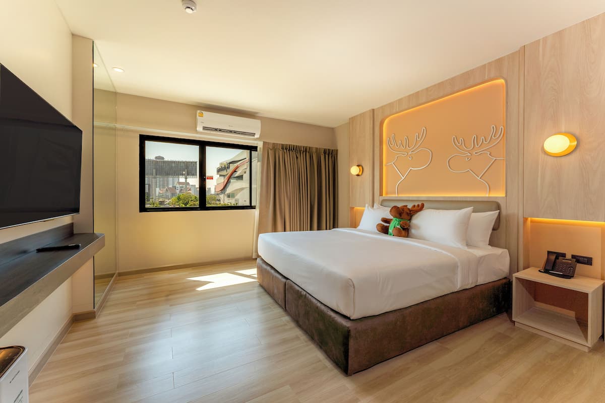 Quarto de hotel moderno com uma cama grande, televisão de tela plana, janela com vista para a cidade e um objeto decorativo na parede.