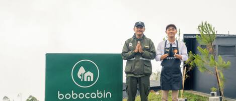 Duas pessoas em frente a uma placa de Bobocabin Kawah Ciwidey.