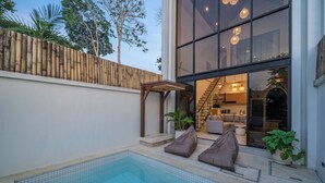 Uma área de piscina moderna ao ar livre, com cerca de madeira, pérgola e escadaria que leva a uma entrada com porta de vidro.