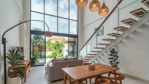 Uma sala de estar ampla com uma mesa de jantar de madeira, um sofá e um lance de escadas com degraus de madeira.
