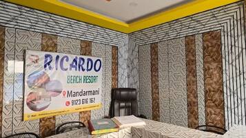 Uma sala de conferências com um banner do Ricardo Beach Resort, uma cadeira de couro preto e papel de parede estampado.