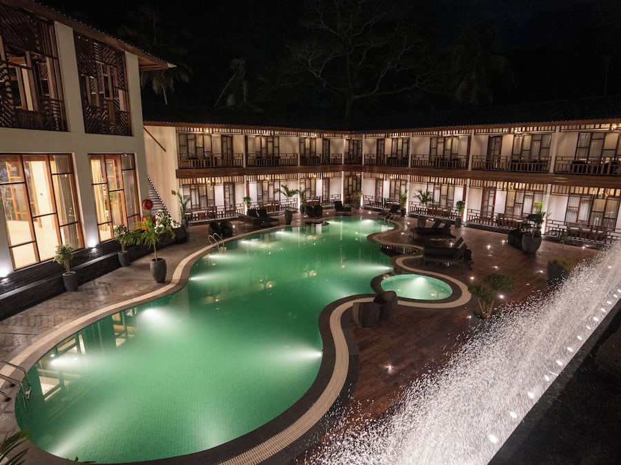 Uma área de piscina à noite, com vários níveis de varandas, uma piscina central e áreas de estar ao redor.