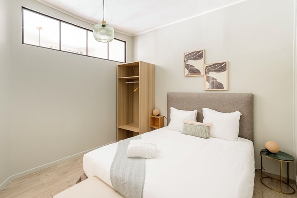 Quarto moderno com uma cama grande, um guarda-roupa de madeira e um candeeiro suspenso.