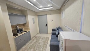 Um espaço compacto com cozinha compacta, um sofá cinzento e uma geladeira branca.
