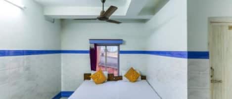 Quarto pequeno com cama de solteiro, ventilador de teto, janela com cortina e porta.
