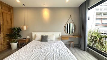 Quarto moderno com cama grande, mesas de cabeceira, luminária suspensa, espelho e vista para o exterior.