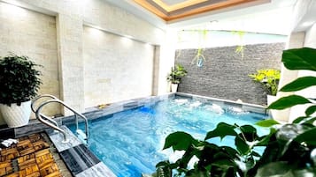 Piscina com área de deck de madeira, cercada por plantas e um muro de pedra.