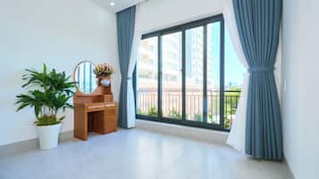 Um quarto espaçoso com uma grande janela, uma escrivaninha de madeira, um vaso com planta e um espelho.