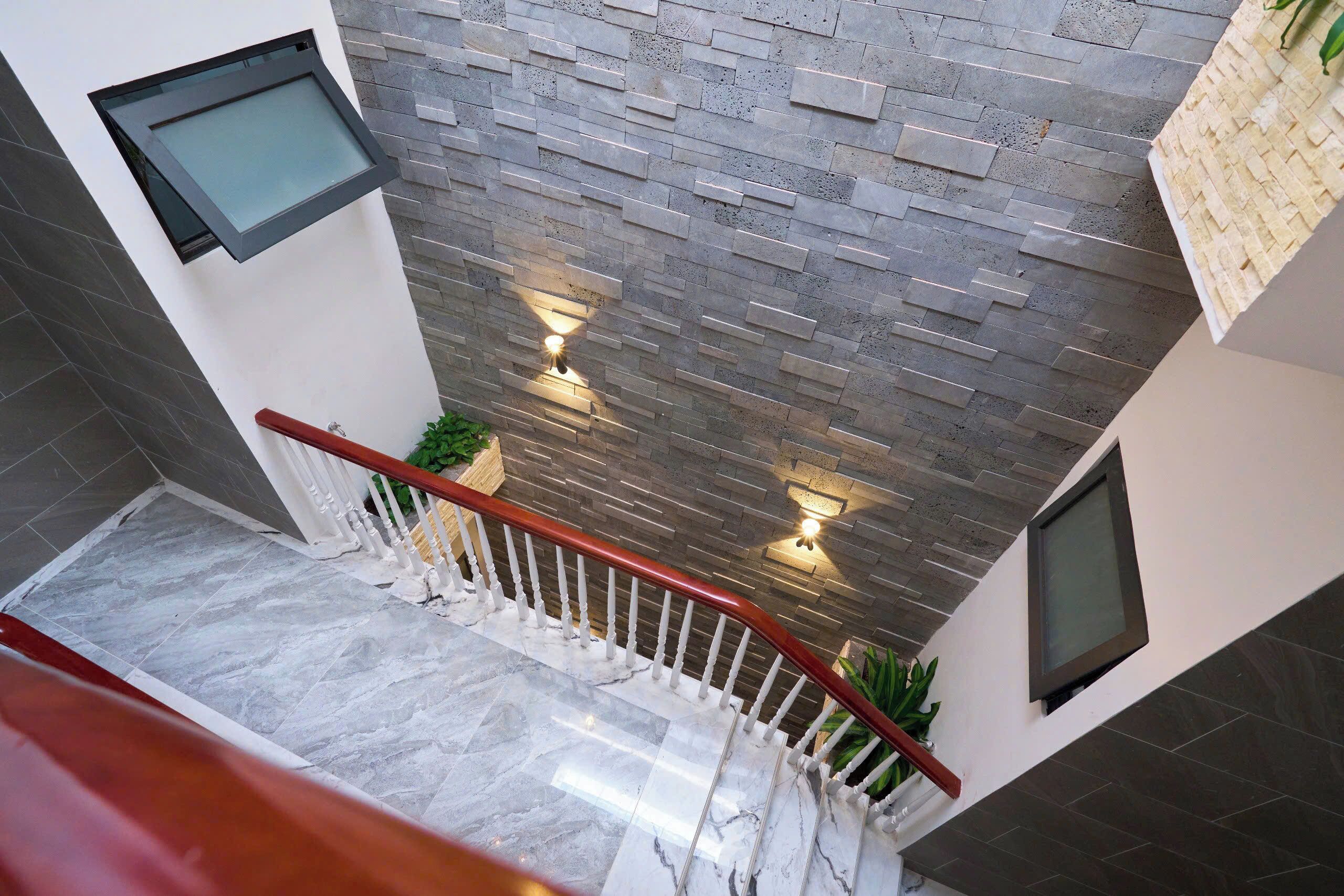 Um interior moderno com escadaria de mármore, parede texturizada e uma pequena planta em vaso.
