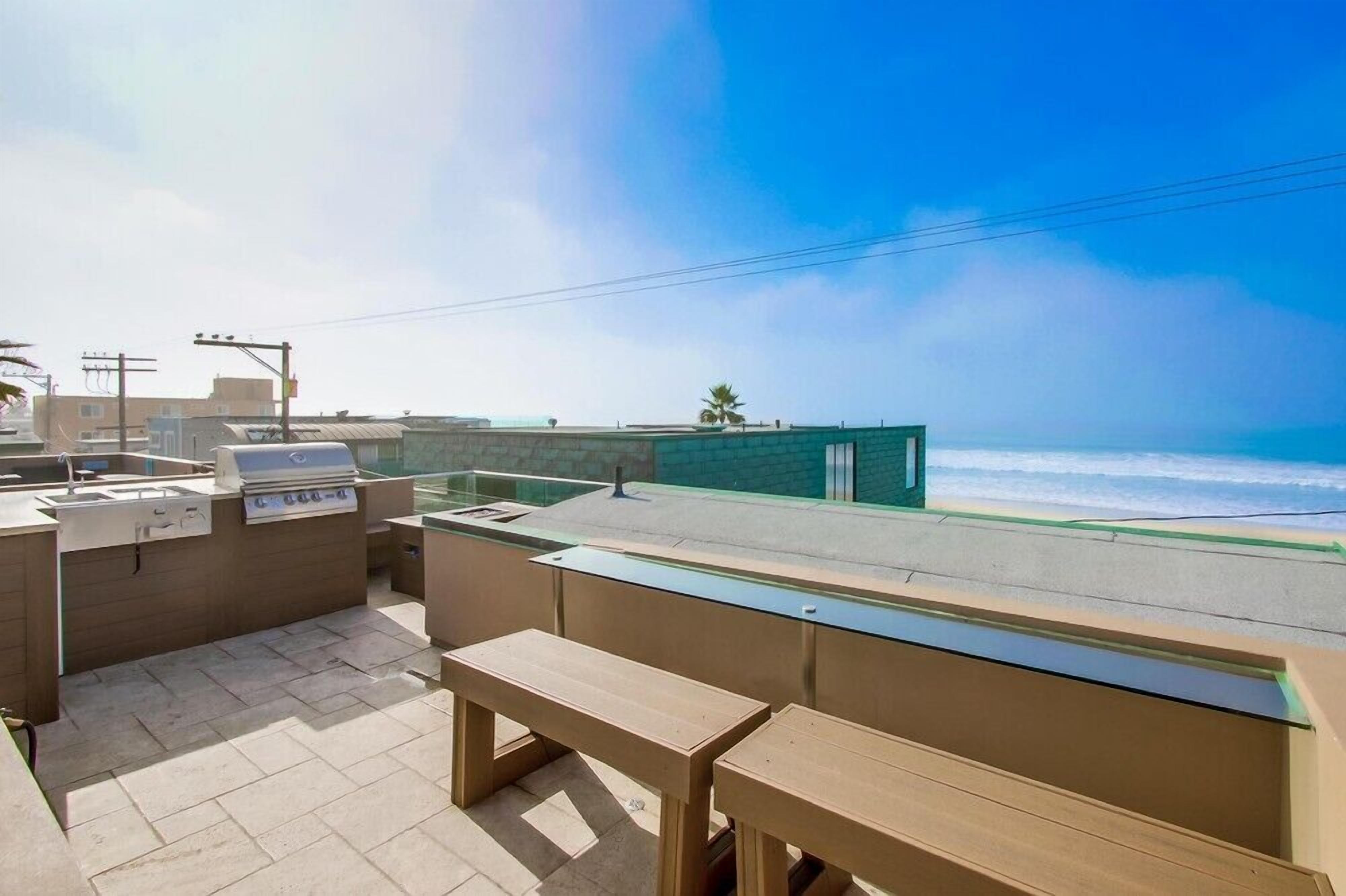 Pátio externo com churrasqueira e área de estar com vista para uma praia.