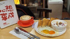 Uma mesa com xícara de café, torrada, ovo e um pote de iogurte com nozes. Há um menu com texto em japonês e uma placa com texto vermelho.