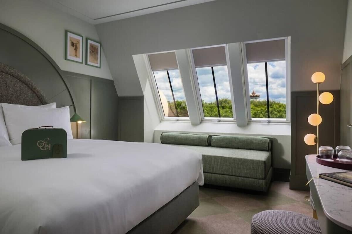Quarto de hotel com cama, área de estar, janela com vista e toucador iluminado.