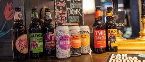 Diversas garrafas e latas de cerveja em um balcão de bar, incluindo marcas como Badger e Outland.