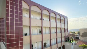 Um edifício de vários andares com fachada em azulejos, varandas com plantas em vasos e um estacionamento à frente.