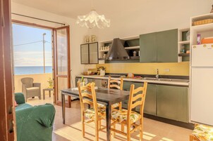 Uma cozinha com vista para o mar, uma mesa de jantar com cadeiras e uma varanda com uma poltrona e um sofá.
