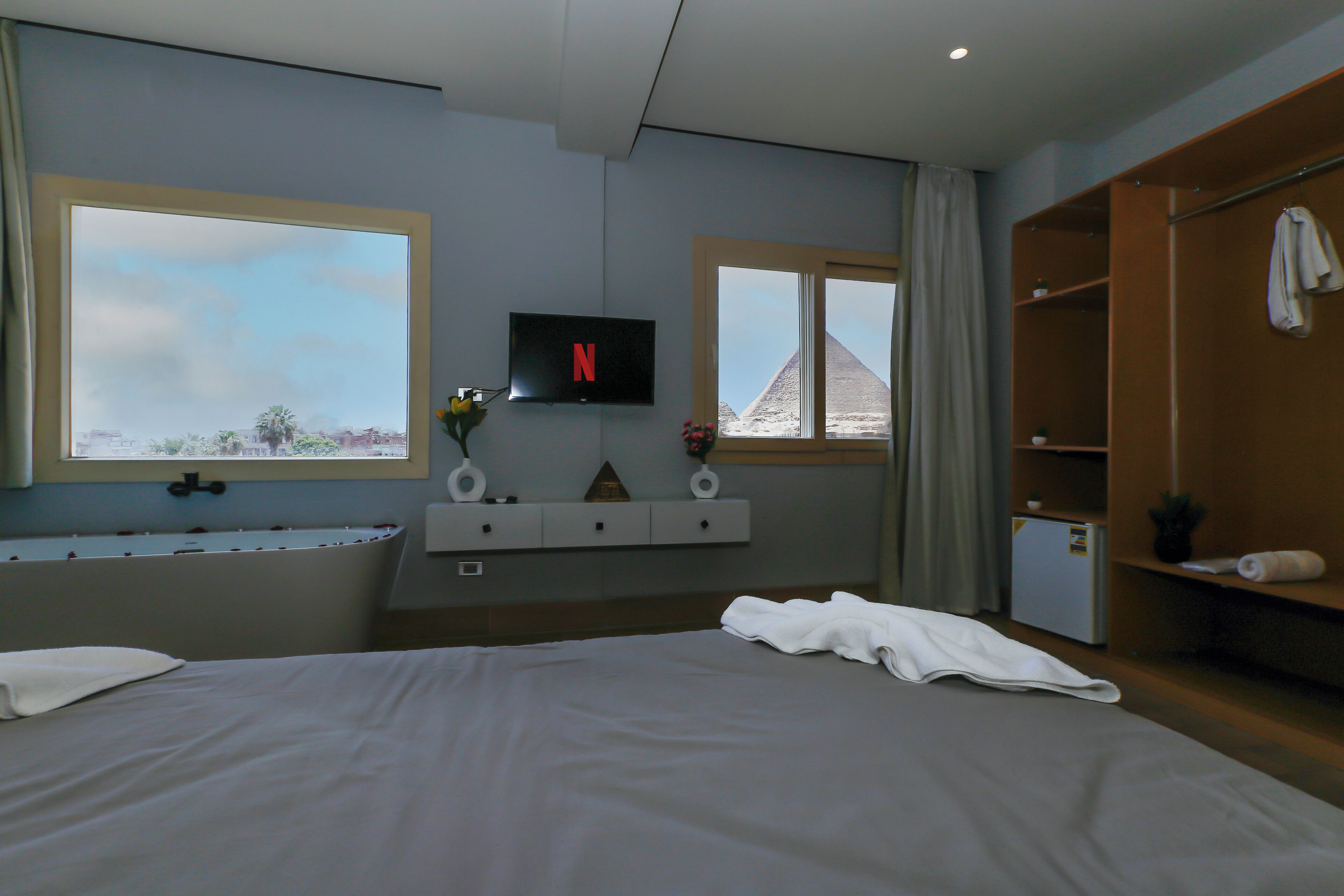 Quarto de hotel com cama grande, televisão fixada na parede, banheira e guarda-roupa.