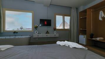 Quarto de hotel com cama grande, televisão fixada na parede, banheira e guarda-roupa.