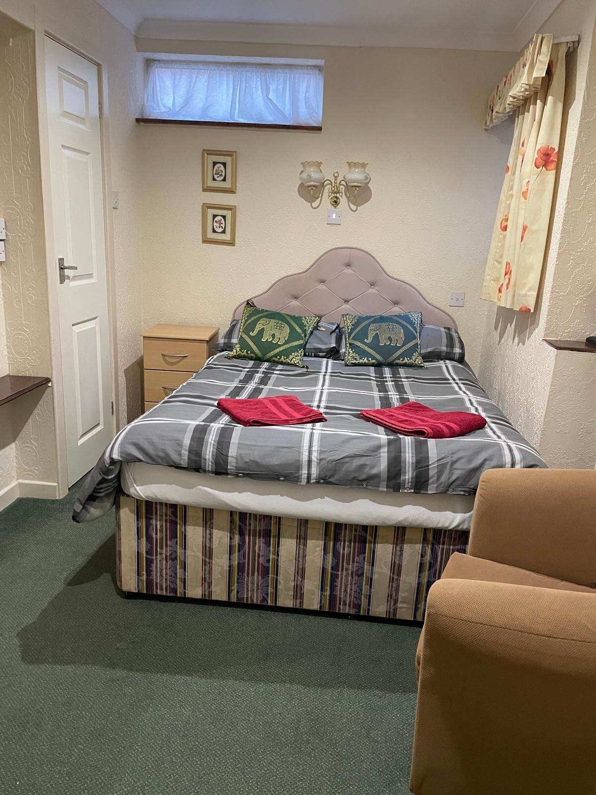 Um quarto com cama, duas mesas de cabeceira, uma janela com cortinas, uma porta e uma cadeira.