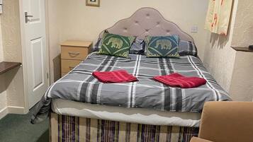 Um quarto com cama, duas mesas de cabeceira, uma janela com cortinas, uma porta e uma cadeira.