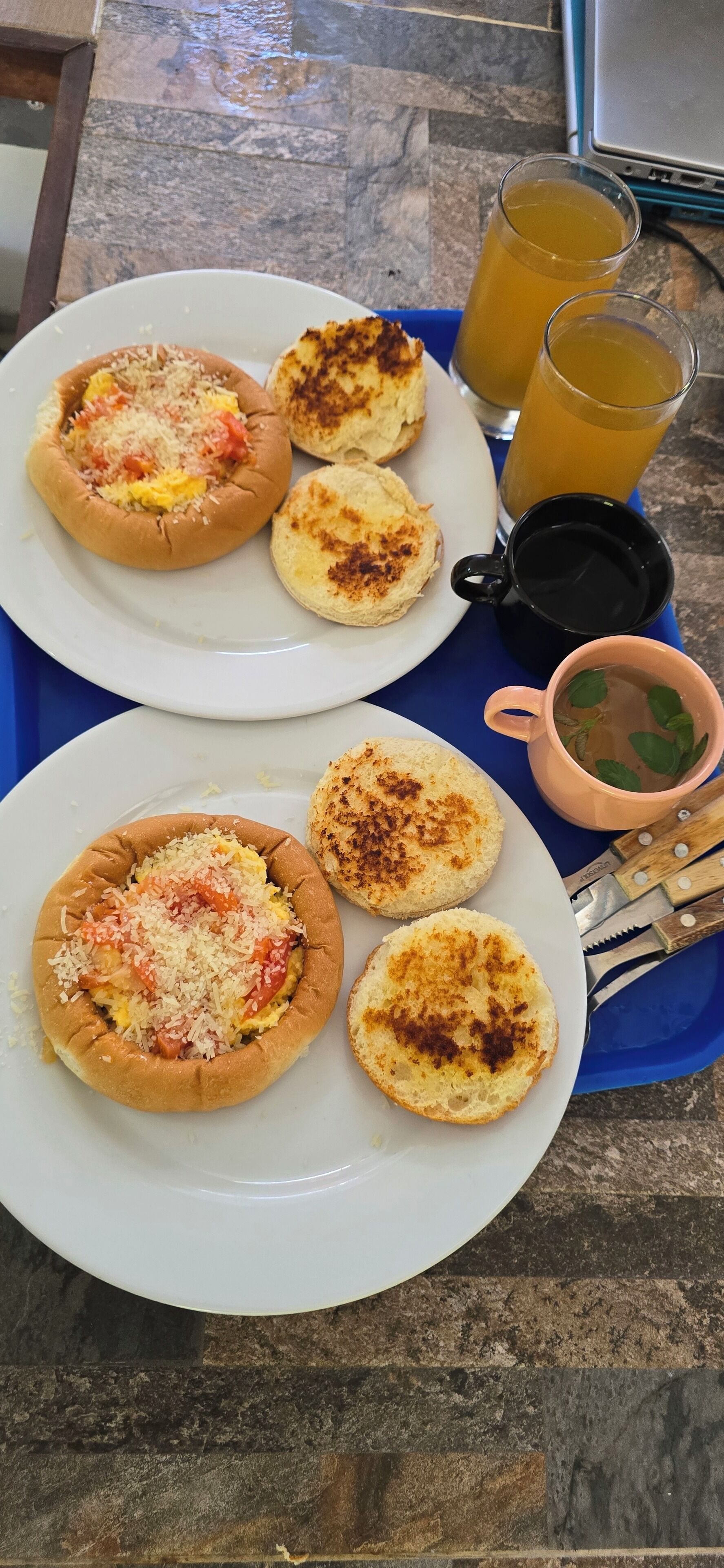 Duas torradas, uma caneca e dois copos de suco de laranja em um tabuleiro, acompanhadas de café da manhã.