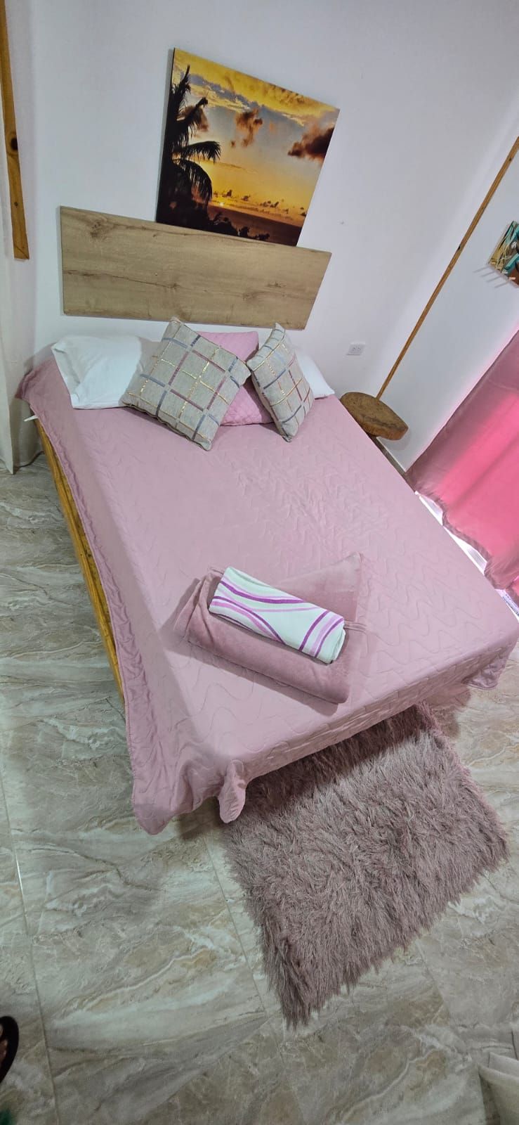 Quarto com cama, cabeceira, quadro, mesa de cabeceira e tapete.