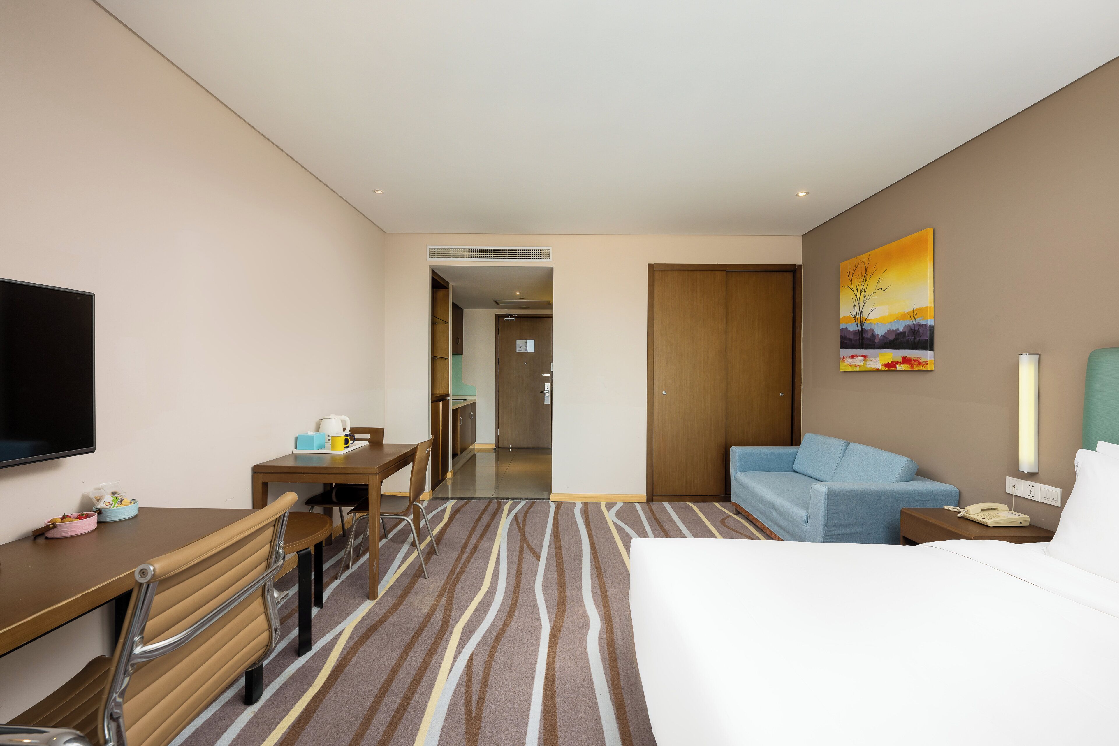 Quarto de hotel com cama, escrivaninha, cadeira, sofá, televisão e um quadro na parede.