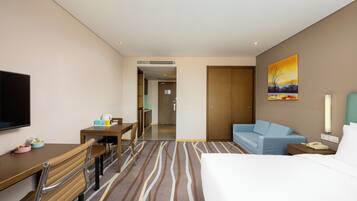 Quarto de hotel com cama, escrivaninha, cadeira, sofá, televisão e um quadro na parede.