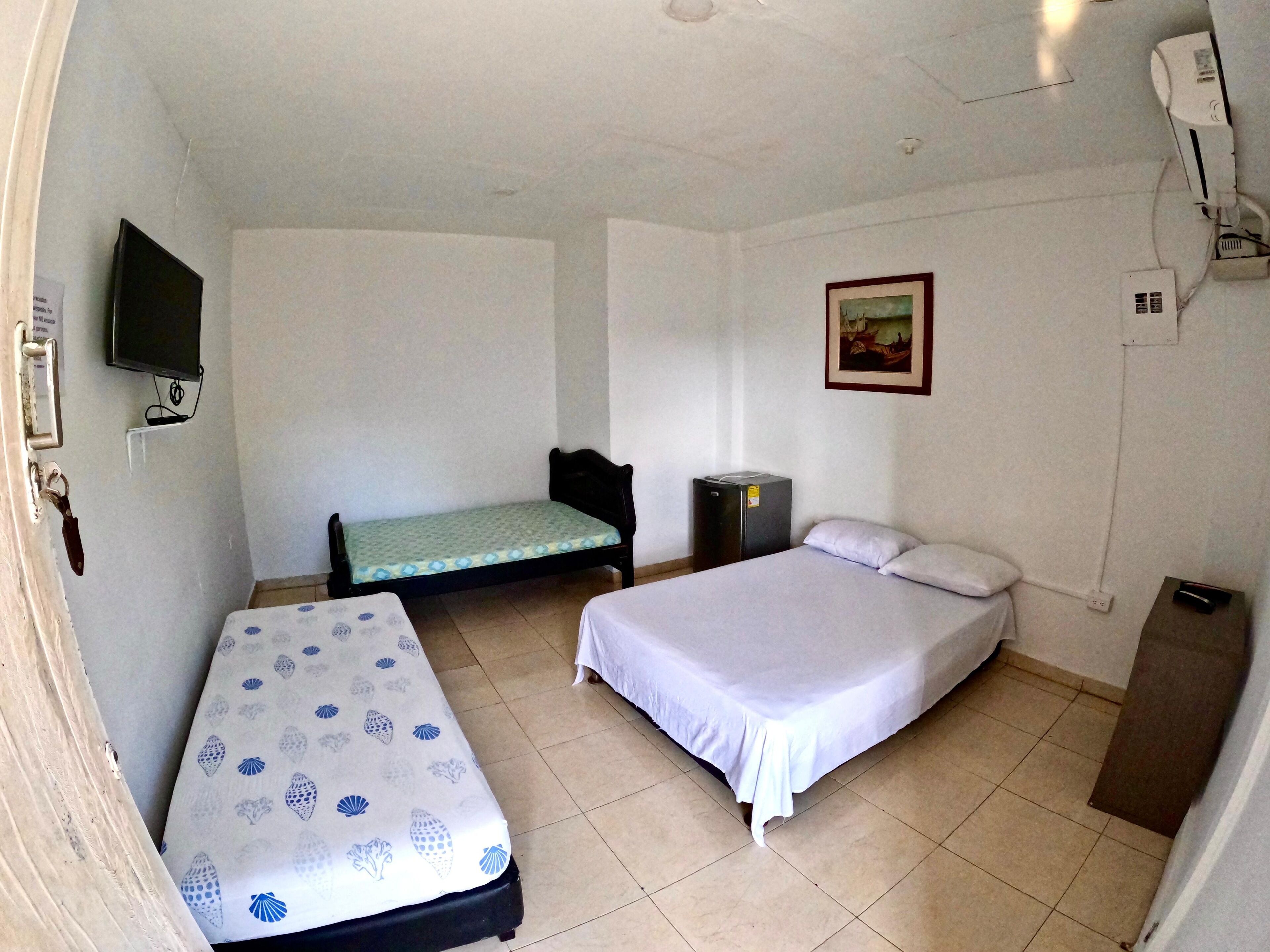 Quarto com duas camas, uma mesa pequena, televisão, um quadro e aquecedor.