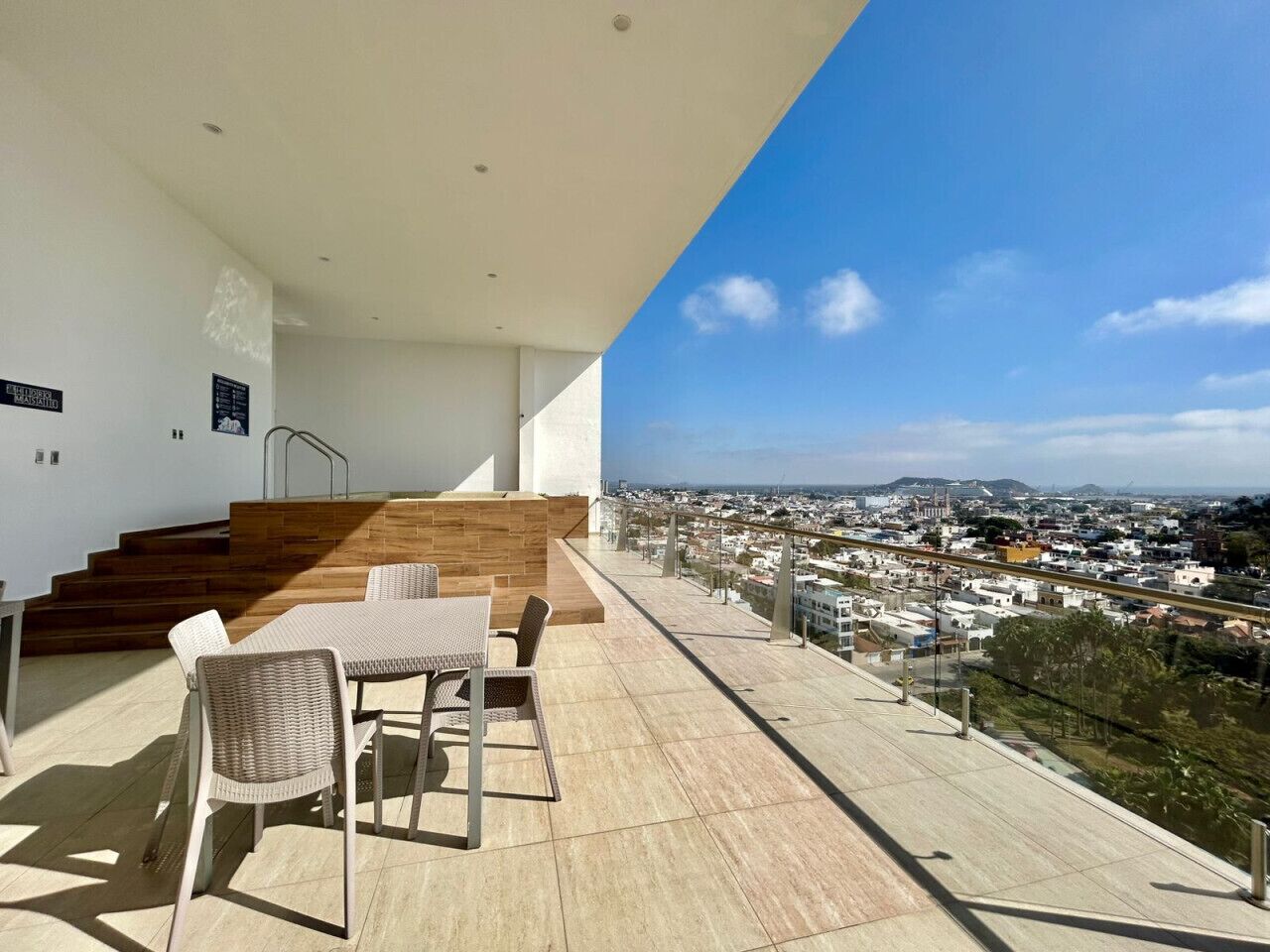 Uma varanda externa moderna com área de refeições, escada e vista para a cidade.