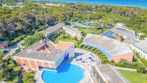 Vista aérea de um resort com piscina central, vários edifícios e vegetação ao redor.