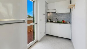 Cozinha moderna com armários brancos, pia de aço inoxidável e janela com vista para uma varanda.