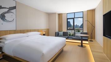 Quarto de hotel moderno com uma cama grande, área de estar com vista e televisão de tela plana.